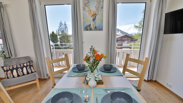 Uma área de refeições com uma mesa posta para dois, um vaso com flores e um quadro na parede.