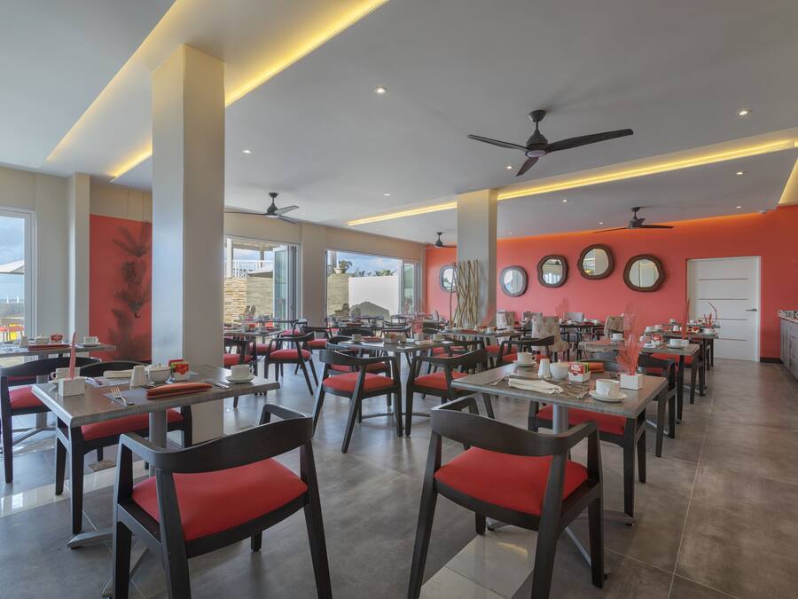 Uma sala de jantar espaçosa com várias mesas e cadeiras, amplas janelas e ventiladores de teto.