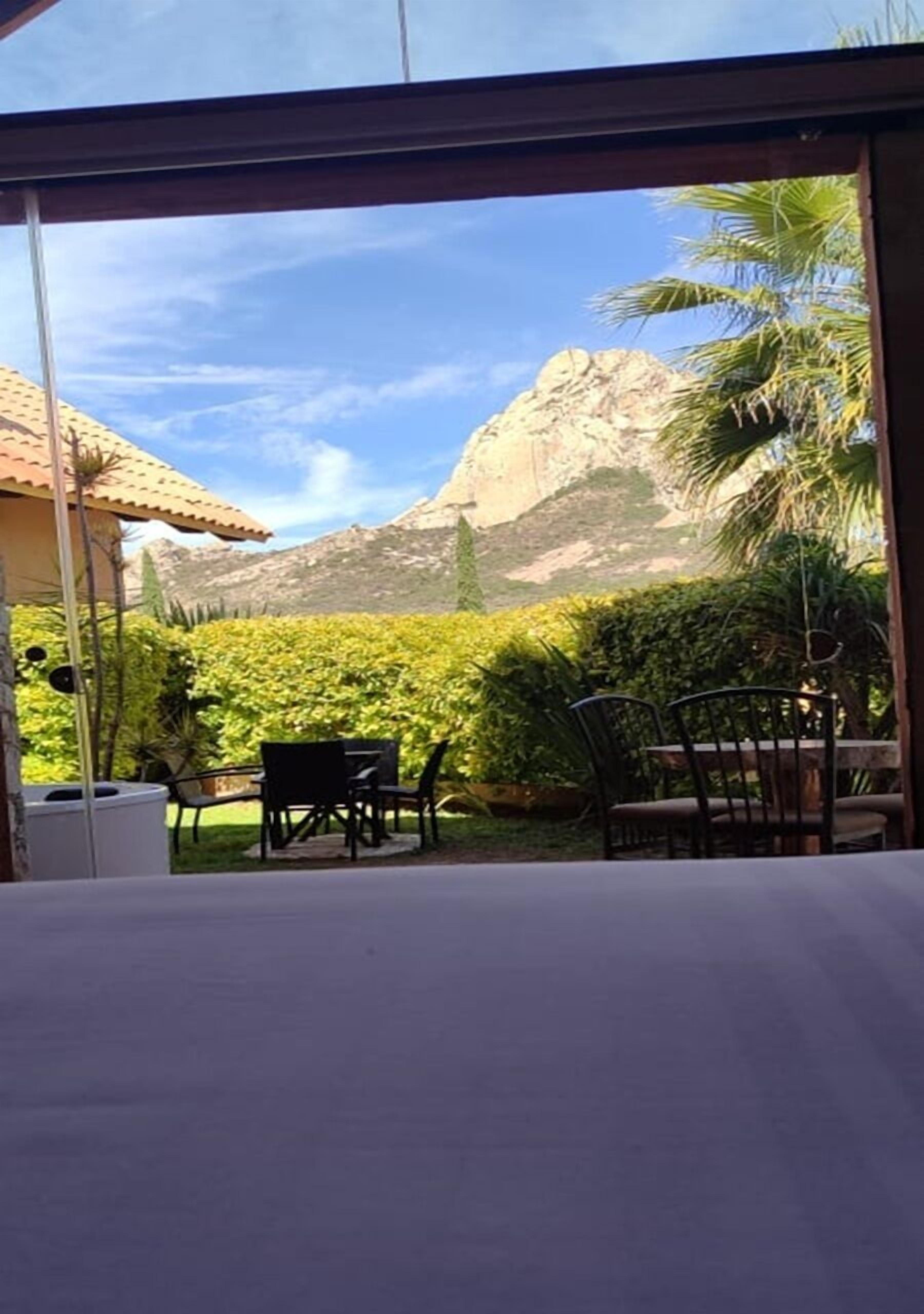 Quarto com vista para uma paisagem montanhosa, área de varanda com mesa e cadeiras e uma janela grande.