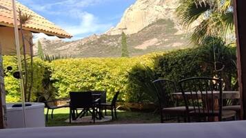 Quarto com vista para uma paisagem montanhosa, área de varanda com mesa e cadeiras e uma janela grande.