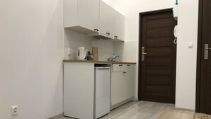 Cozinha compacta com armários brancos, máquina de lavar louça embutida e porta de madeira escura.