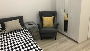 Quarto com cama, cadeira, mesinha e guarda-roupa.