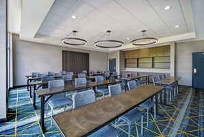 Sala de conferência com mesas e cadeiras, carpete estampado e teto com iluminação embutida.