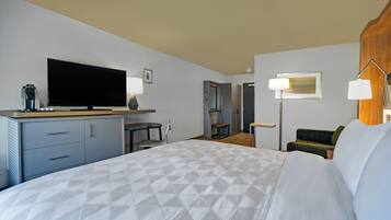 Quarto de hotel com uma cama grande, televisão de tela plana, escrivaninha com luminária, cadeira e guarda-roupa.