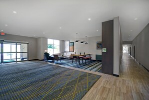 Um quarto espaçoso com uma grande janela, área de jantar com mesa e cadeiras, e piso coberto por carpete.