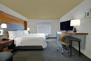Quarto de hotel com cama, escrivaninha, cadeira, televisão, abajur e obras de arte na parede.