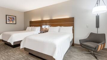 Quarto de hotel com duas camas, uma cadeira moderna, uma luminária e um quadro pendurado na parede.