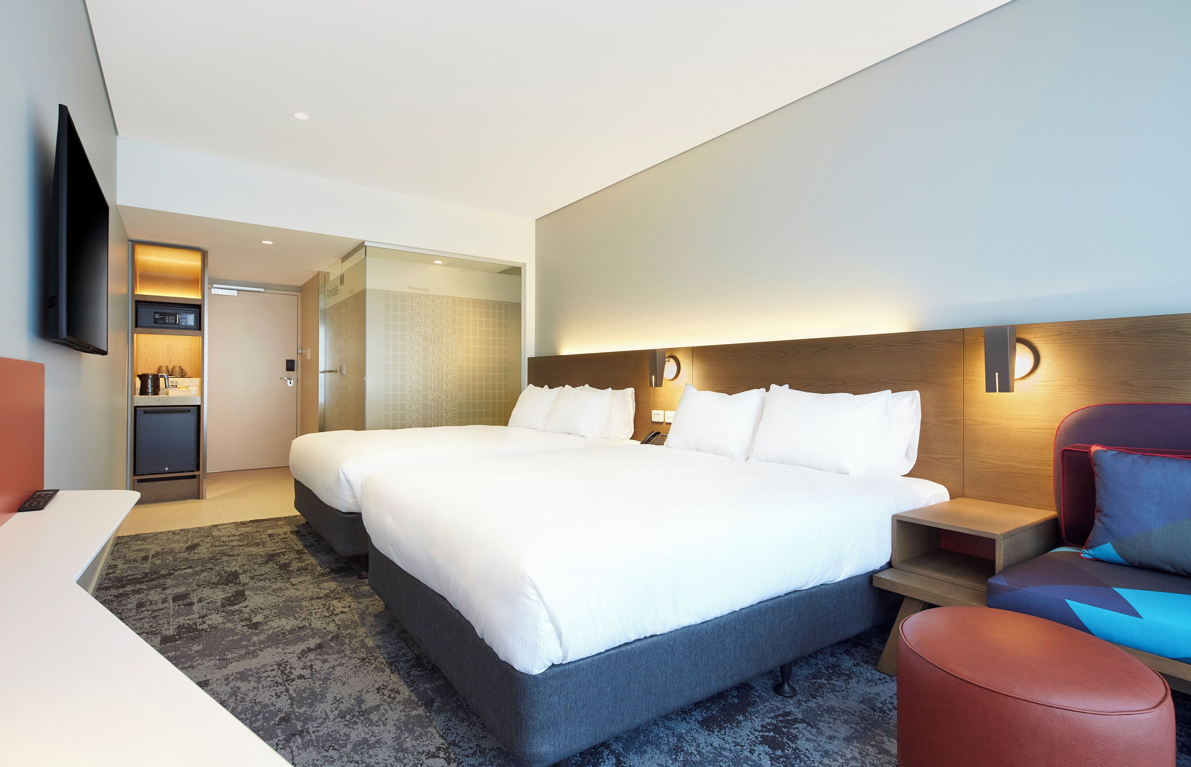 Quarto de hotel moderno com uma cama grande, mesas de cabeceira, televisão e área de chuveiro.