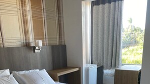 Cama bem arrumada em quarto de hotel com vista para o verde lá fora.