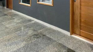 Um corredor com paredes escuras, três grandes janelas com molduras de madeira e uma porta de madeira com painéis horizontais.