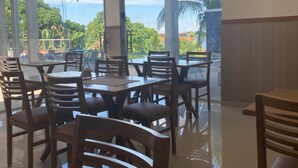Uma ampla área de jantar com grandes janelas que oferecem vista para palmeiras e um céu claro.