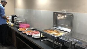 Disposição de buffet com diversos alimentos e uma pessoa servindo.