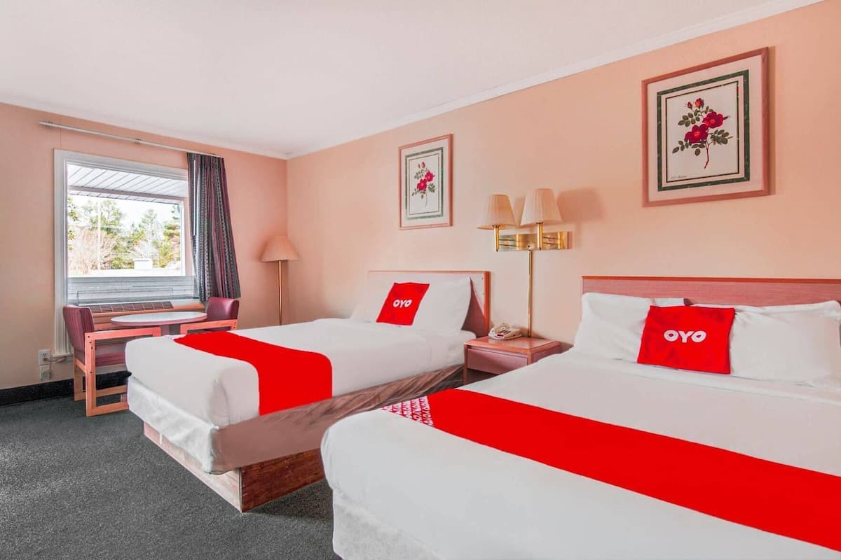 Quarto de hotel com duas camas, uma escrivaninha e uma janela com cortinas.