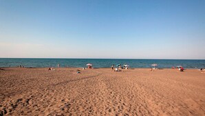 Uma extensa praia de areia com águas azul-claras, guarda-sóis e pessoas relaxando.