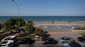 Uma área de estacionamento com carros, uma estrada que leva à praia e uma vista desobstruída do oceano.