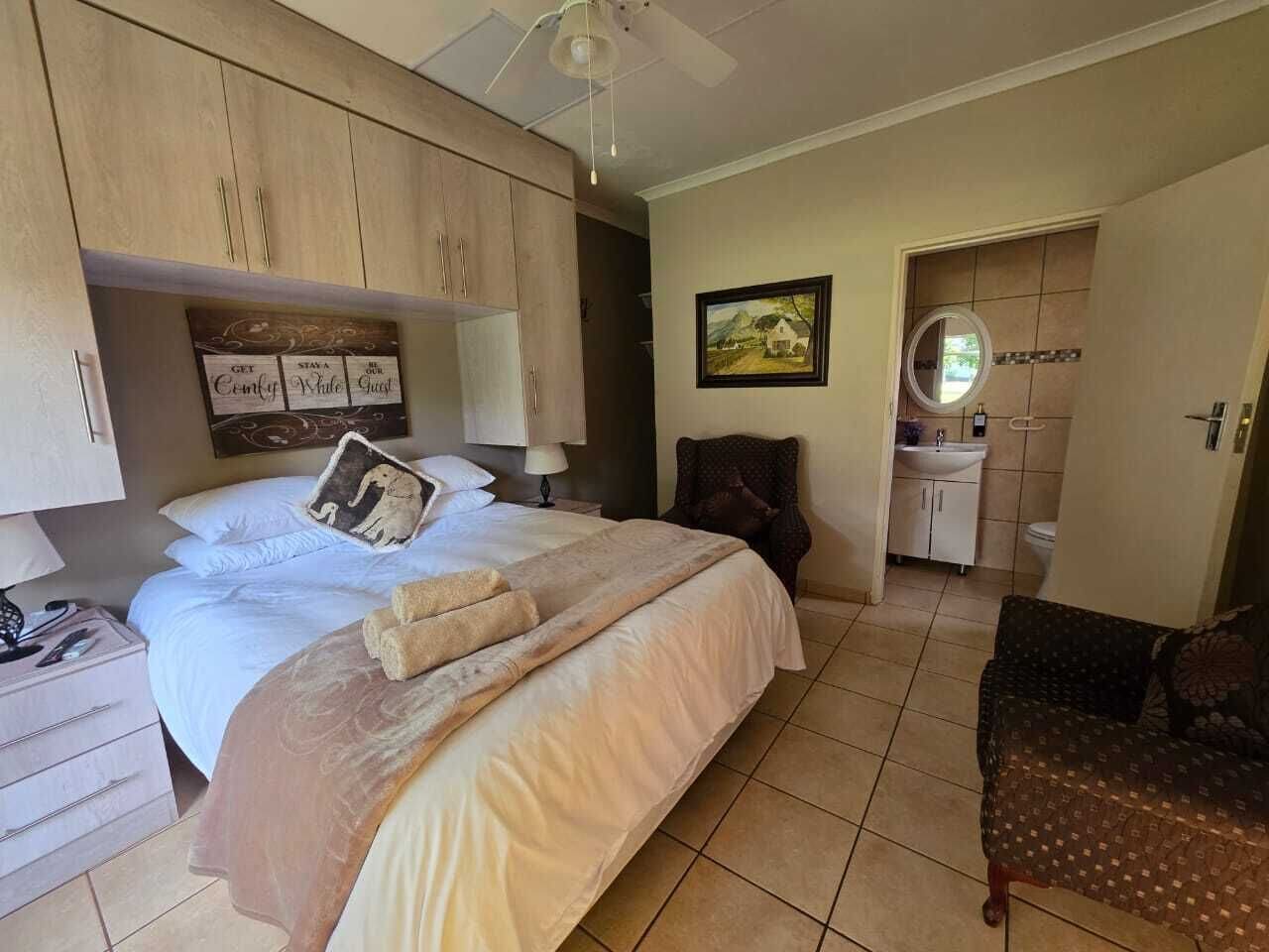 Quarto de hotel com cama, cadeira, escrivaninha, guarda-roupa e banheiro.