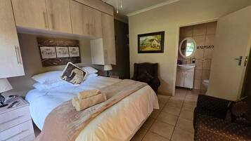 Quarto de hotel com cama, cadeira, escrivaninha, guarda-roupa e banheiro.