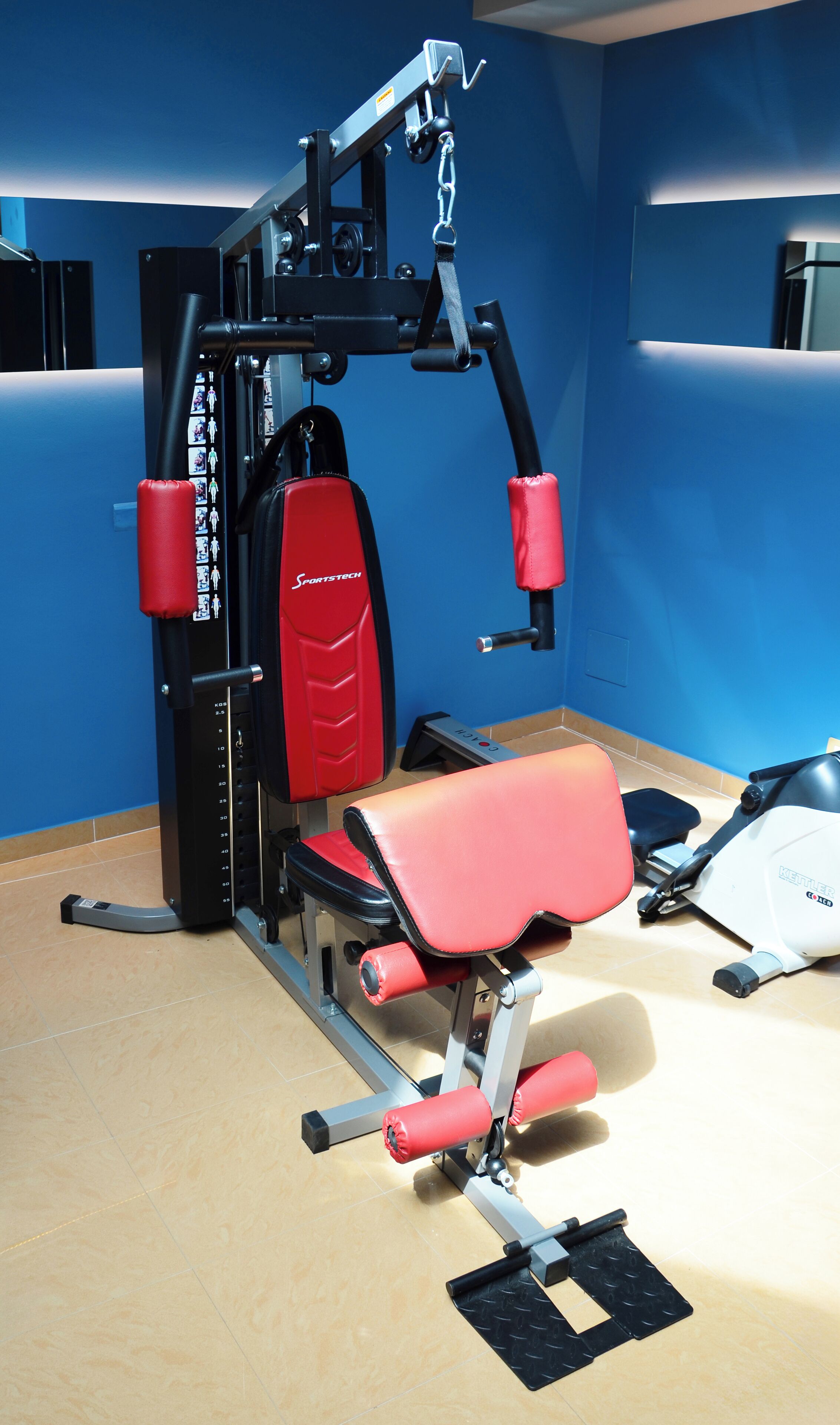 Uma academia com equipamentos nas cores vermelho e preto, um banco e um kettlebell.