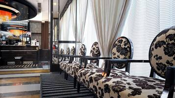 Um saguão de hotel com uma fileira de sofás e cadeiras, uma recepção e um espaço de bar.