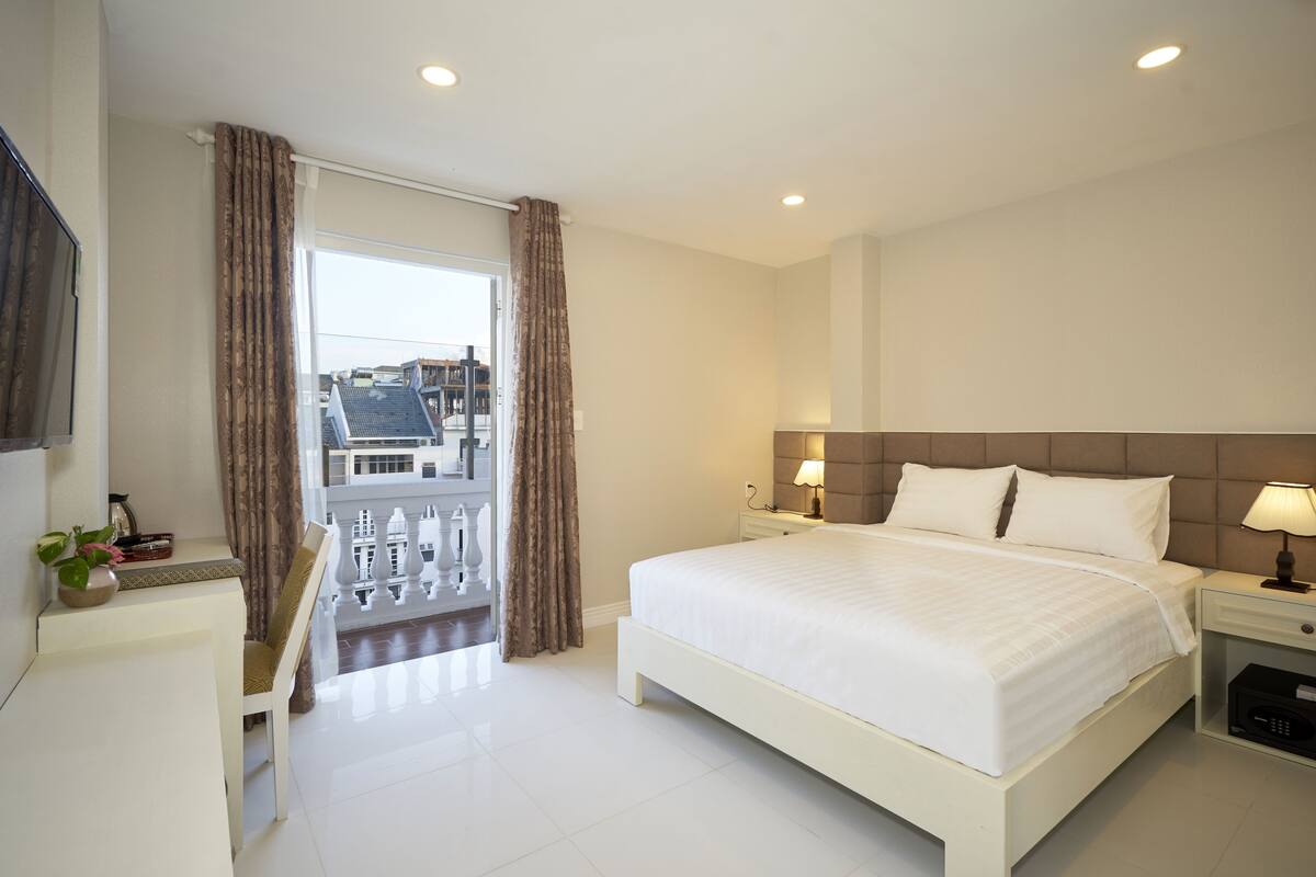 Quarto de hotel com uma cama grande, uma escrivaninha e vista para uma varanda com guarda-corrimão.