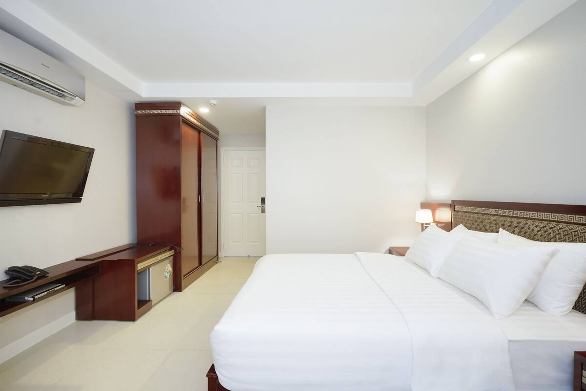 Quarto de hotel com cama, televisão, secretária e telefone, guarda-roupa e porta.
