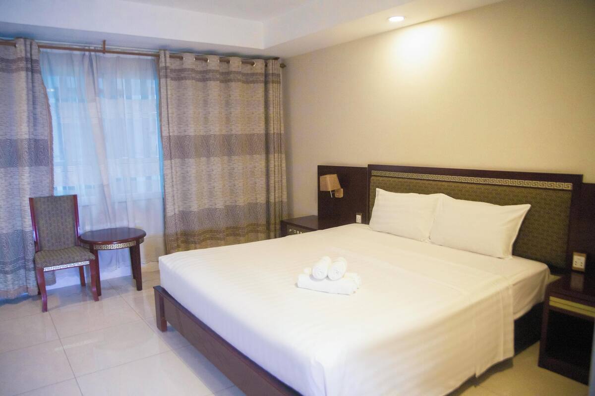Quarto de hotel com uma cama grande, uma cadeira, uma mesa de cabeceira e um abajur.