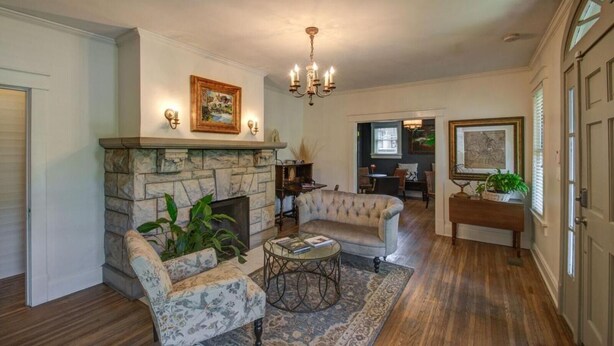 Uma sala de estar com lareira de pedra, dois poltronas, uma mesa de centro e um candelabro.