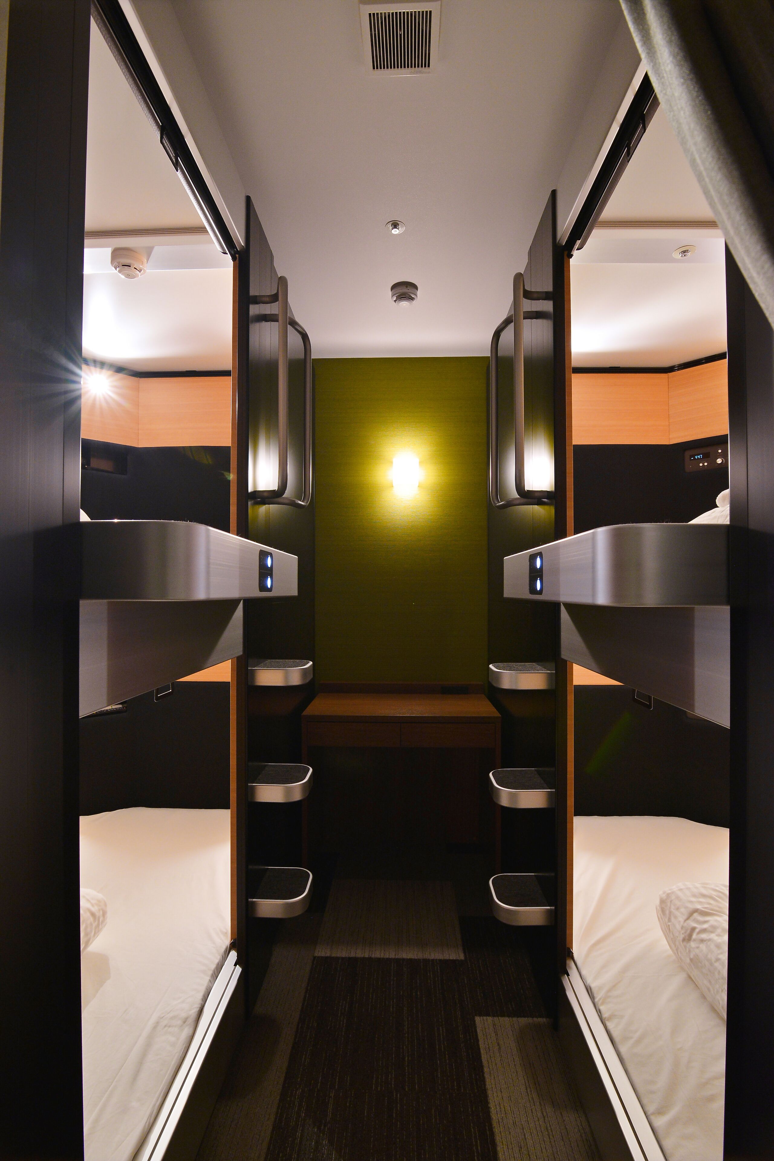 Quarto de hotel compacto com beliches, um pequeno espaço de estar e uma televisão fixada na parede.