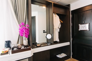 Quarto de hotel com toucador, espelho, roupão pendurado, chinelos e pequena mesa com um vaso de flores.