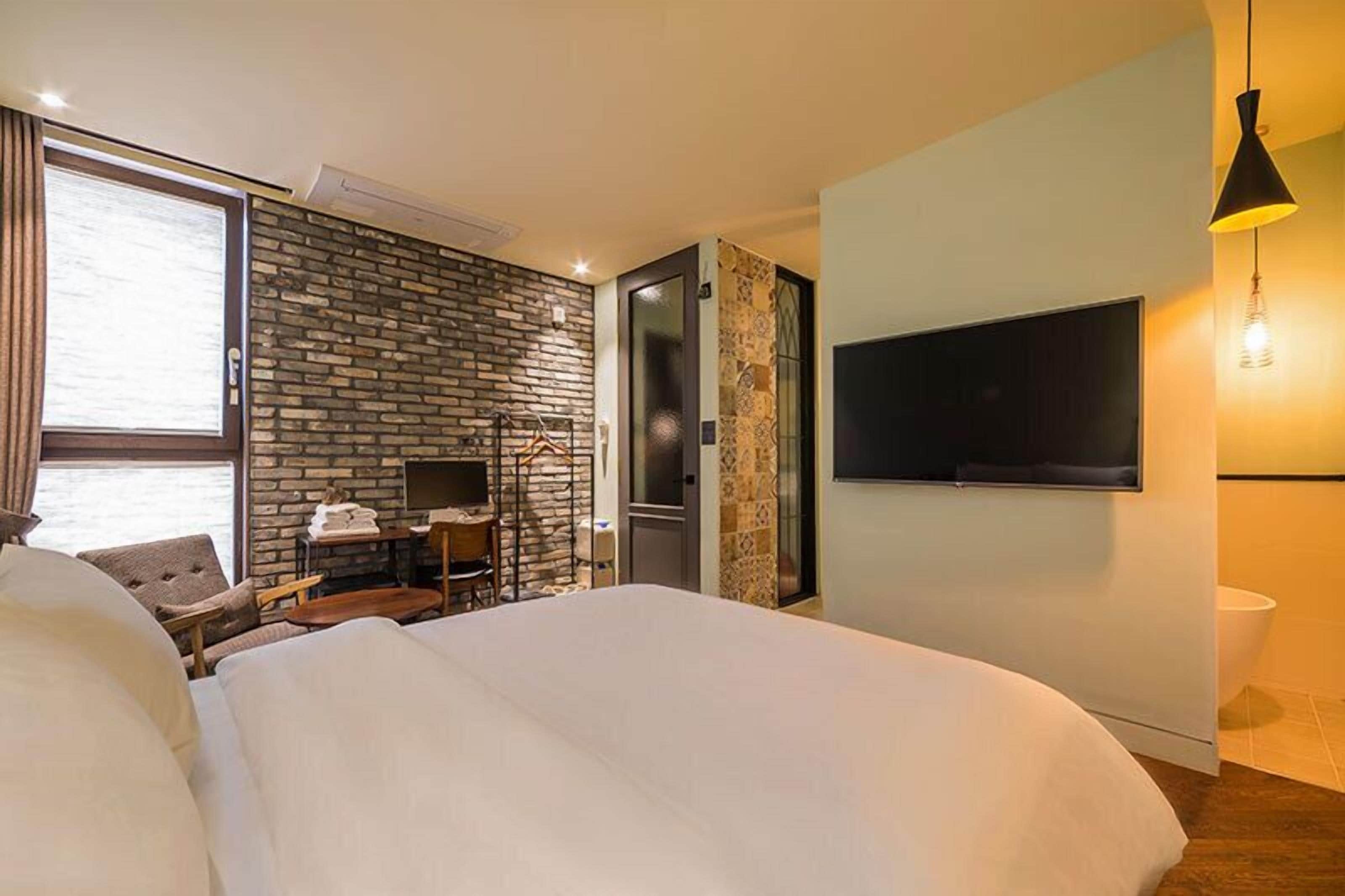 Quarto de hotel com uma cama grande, televisão na parede, secretária com uma cadeira e parede de pedra.