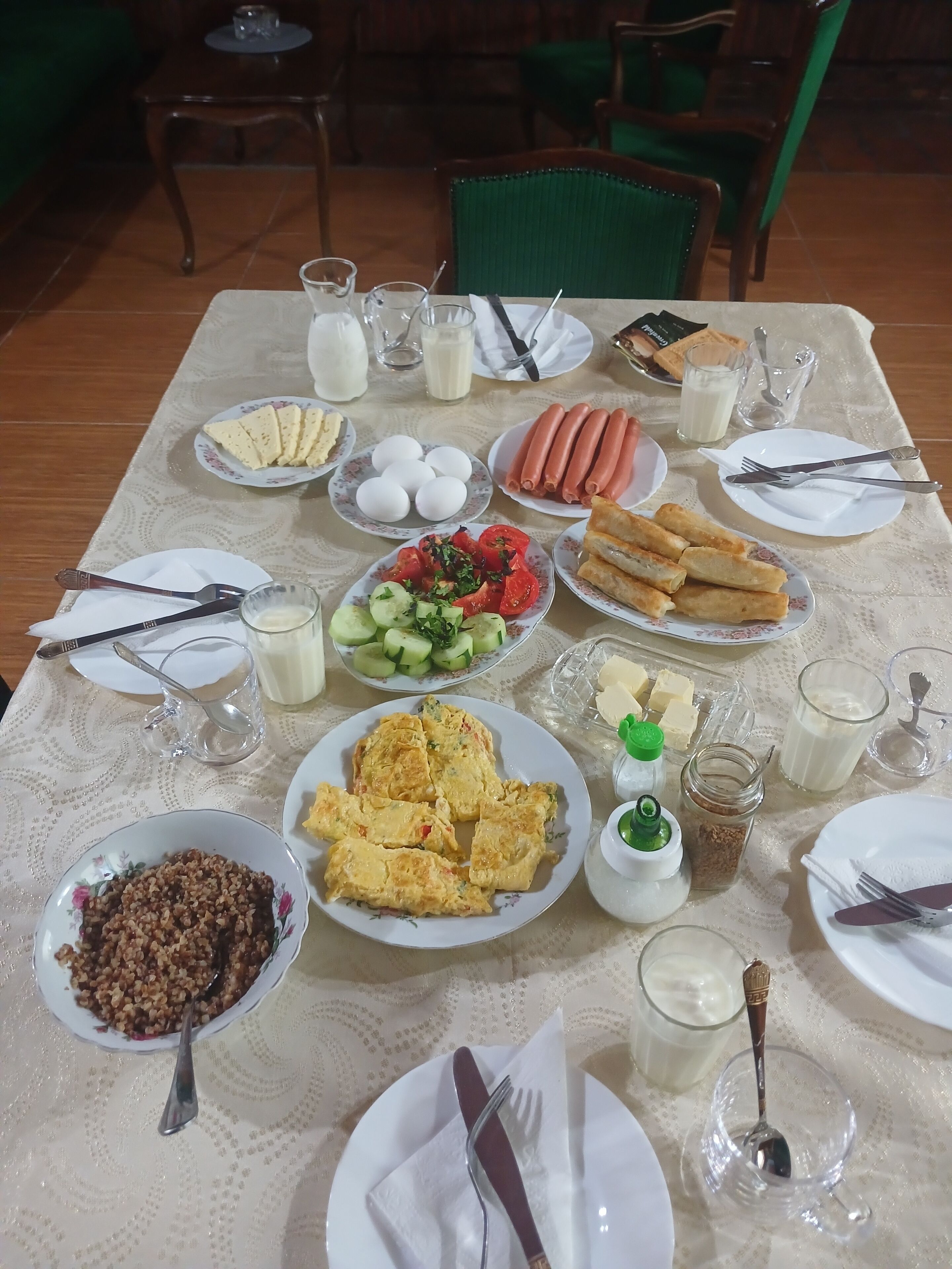 Uma mesa de jantar posta com vários pratos, incluindo ovos, salsichas e uma salada.