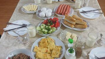 Uma mesa de jantar posta com vários pratos, incluindo ovos, salsichas e uma salada.