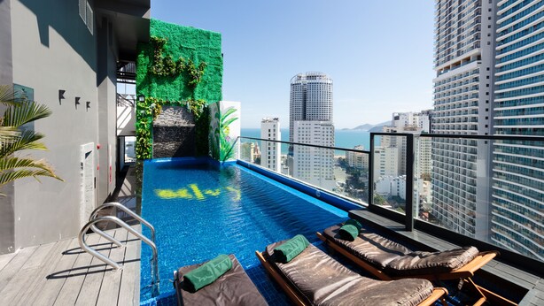 Piscina infinita no terraço com espreguiçadeiras e uma parede verde.