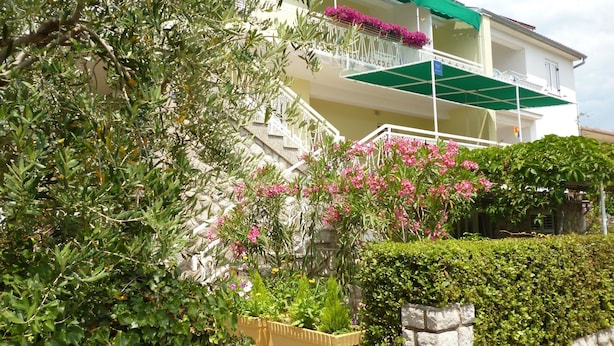 Um hotel com varanda, flores cor-de-rosa, parede de pedra e toldo verde.