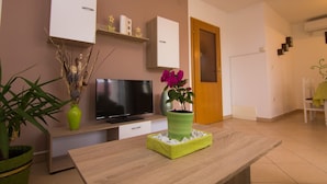 Uma sala de estar moderna com uma TV de tela plana, uma mesa de centro de madeira e um vaso verde com flores.