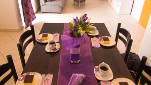 Uma área de refeições com uma mesa posta para dois, incluindo pratos, talheres e um vaso de flores.