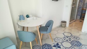 Uma pequena área de refeições com uma mesa branca e duas cadeiras azuis, uma chaleira e um conjunto de chá sobre a mesa.