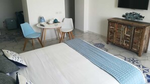 Quarto de hotel com cama, secretária com cadeiras, televisão e armário.