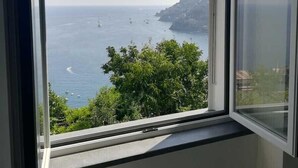 Uma janela com vista para o mar, barcos e vegetação.