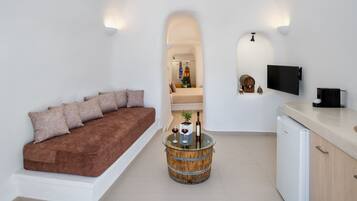 Uma sala de estar moderna com sofá, mesa de centro de vidro, televisão e cozinha.