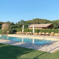 Área da piscina com espreguiçadeiras e um edifício ao fundo.