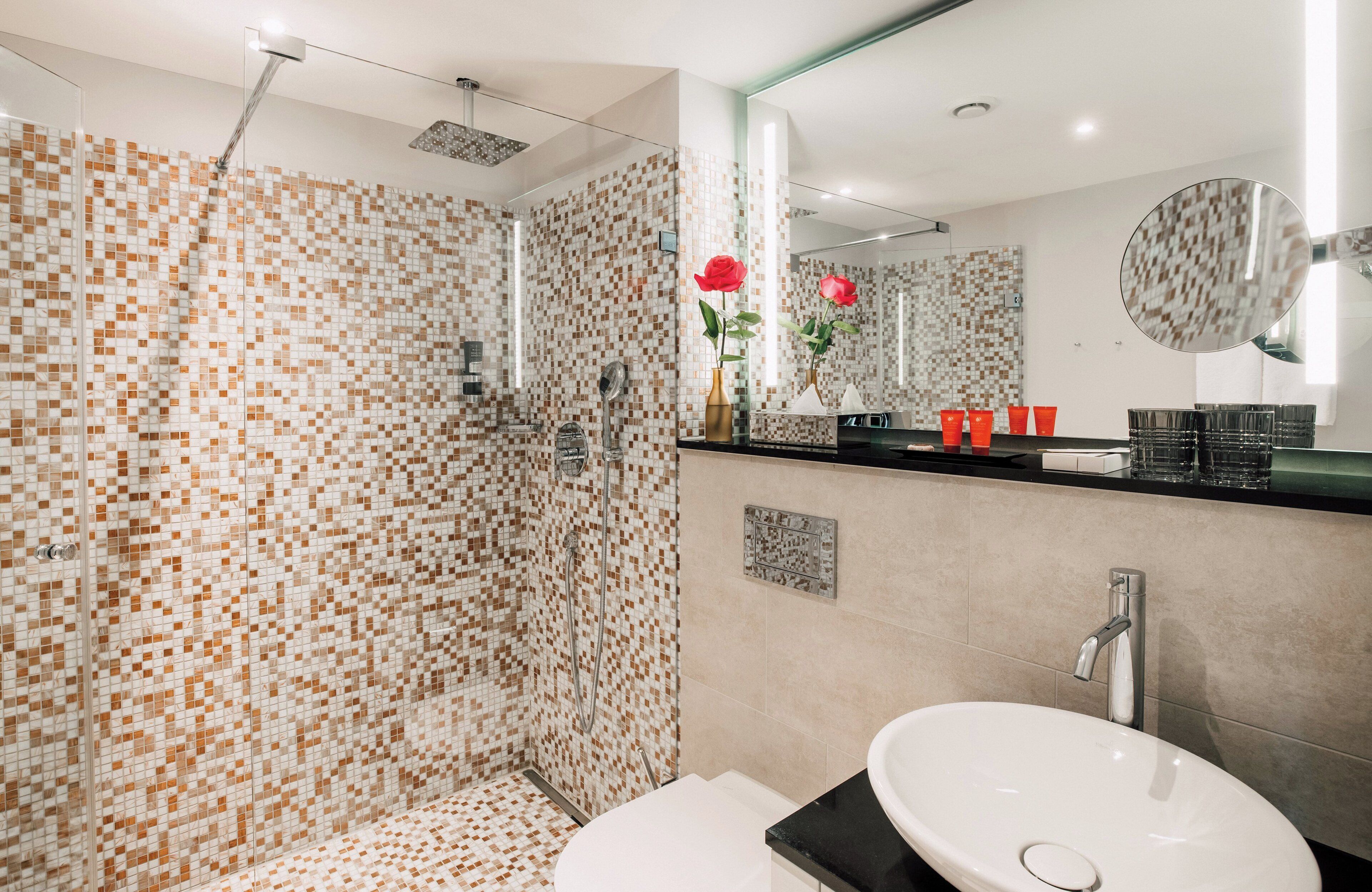 Um banheiro moderno com parede de chuveiro em mosaico, um espelho grande e uma pia com bancada preta.
