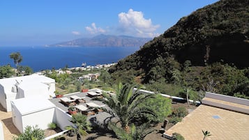 Terraço no terraço com mesas ao ar livre, uma palmeira e vista para o mar e montanhas ao longe.