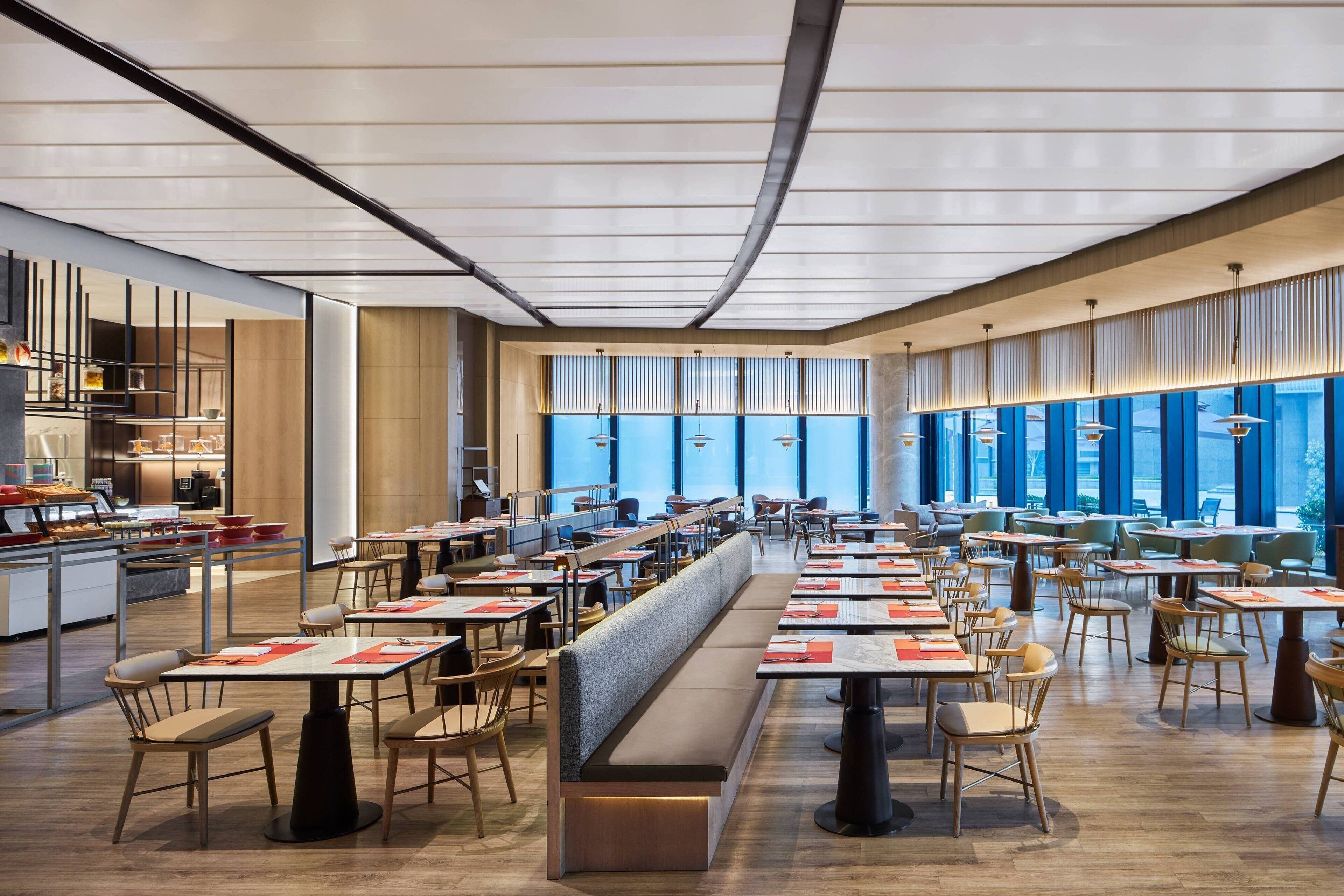 Um restaurante moderno com um balcão extenso, várias mesas e um pé-direito alto com grandes janelas.
