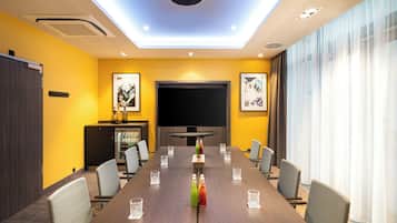 Uma sala de conferências com uma mesa comprida, cadeiras, uma tela de projetor e quadros nas paredes.