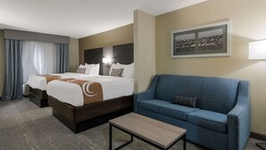 Quarto de hotel com duas camas, um sofá azul, uma mesinha e um quadro na parede.