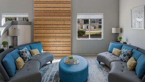 Sala de estar moderna com dois sofás cinzas, um banquinho azul e um painel de ripas de madeira.