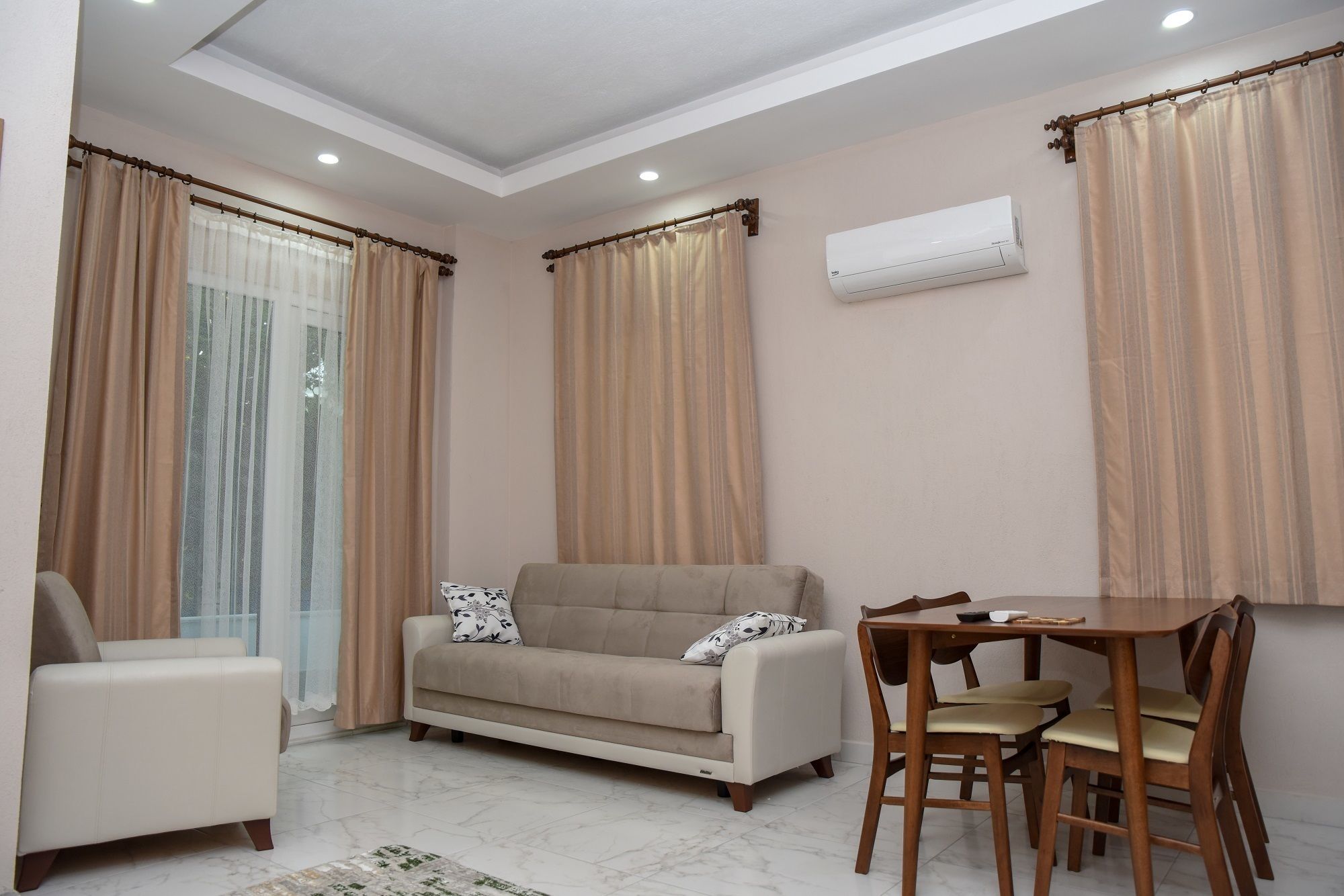 Uma sala de estar com um sofá, uma mesa de jantar com cadeiras e uma janela com cortinas.