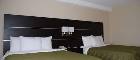 Quarto de hotel com duas camas, cada uma com colcha verde, cabeceira escura e duas luminárias fixadas na parede.