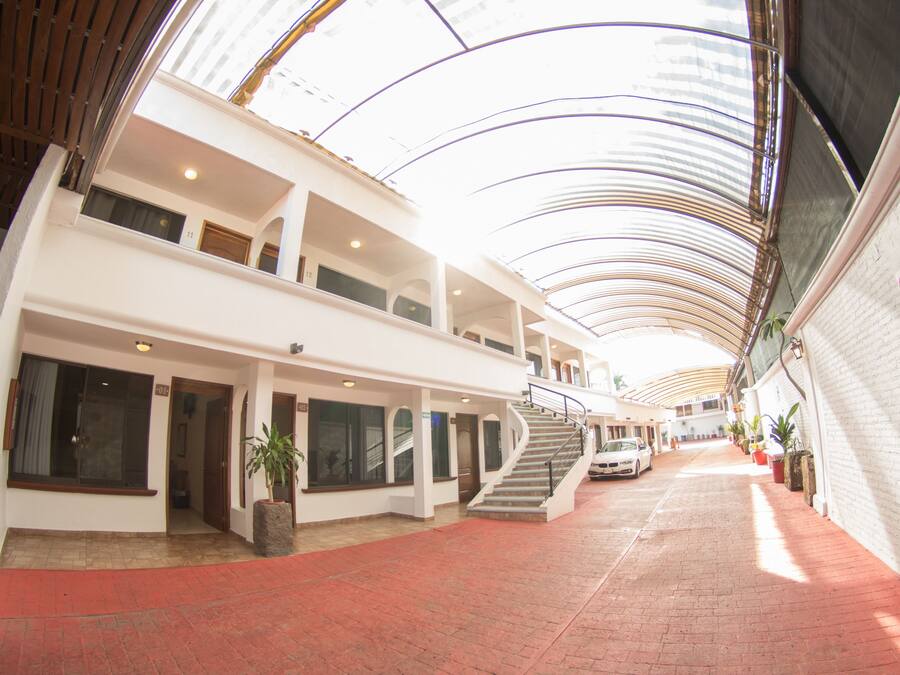 Um corredor amplo e interno com piso de tijolos vermelhos, uma escada e um edifício branco com várias janelas e portas.